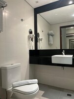 Uma casa de banho moderna com sanita, lavatório e secador de cabelo fixado na parede.