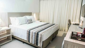 Quarto de hotel com cama, mesa de cabeceira e escrivaninha com um laptop.