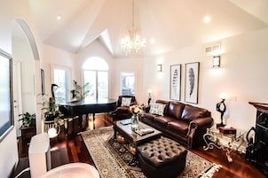 Uma sala de estar ampla com um piano de cauda, sofá de couro e um lustre.