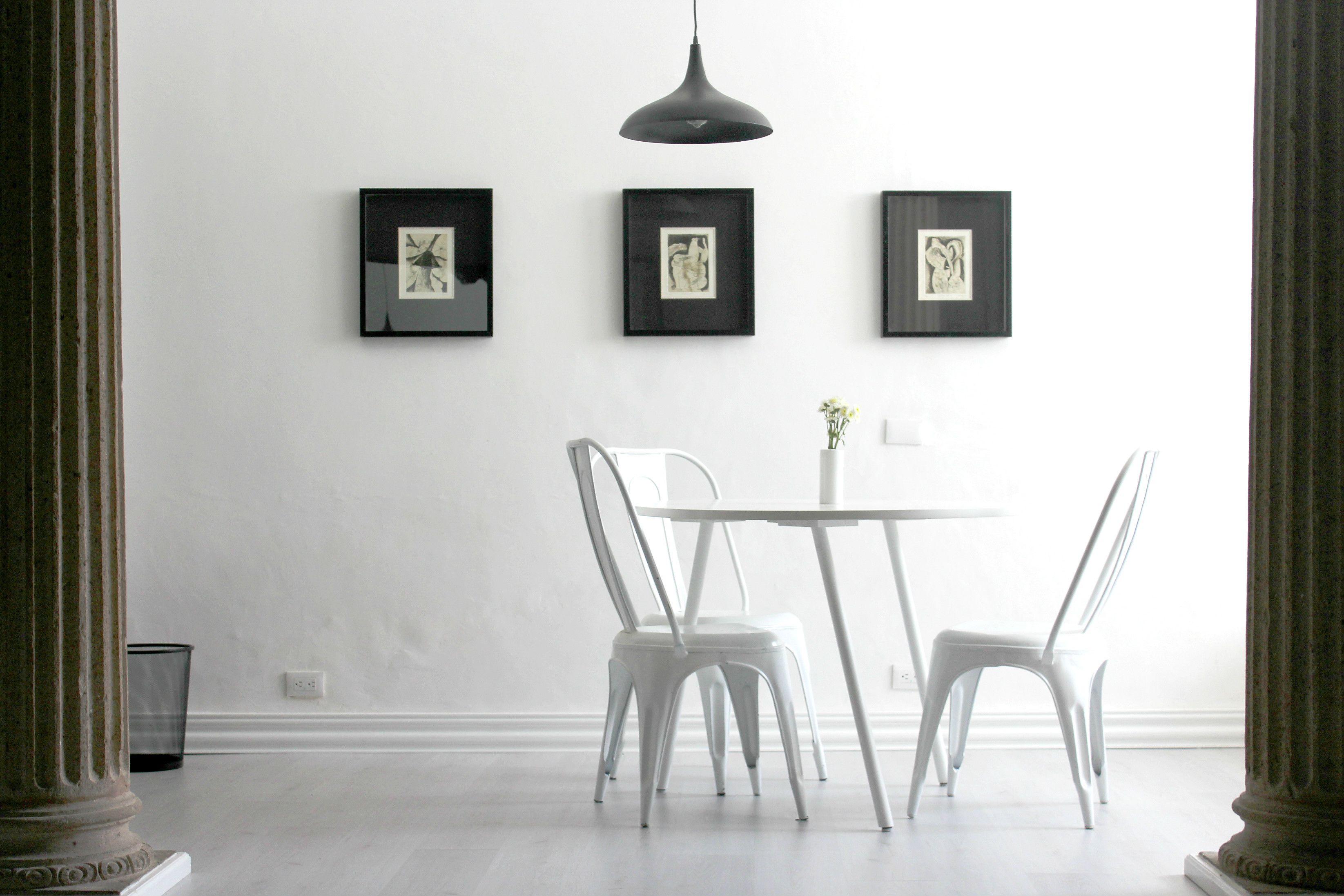 Uma área de refeições com uma mesa e cadeiras brancas, obra de arte enquadrada na parede e uma luminária pendente.