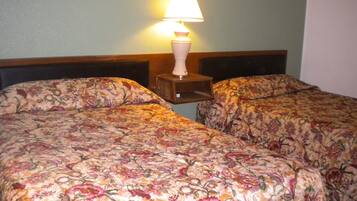 Quarto de hotel com duas camas, cada uma com roupa de cama estampada com motivos florais, uma mesa de cabeceira com luminária e cabeceira de madeira.