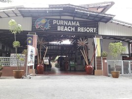 A entrada do Purnama Beach Resort, com uma galeria coberta, plantas em vasos e uma placa com o nome do resort.