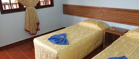 Quarto de hotel com duas camas, cabeceira de madeira, janela com cortinas e chão ladrilhado.