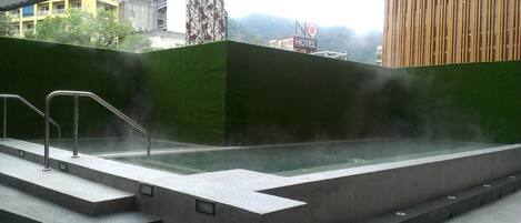 Área de águas termais com piscina, escadas e vista para edifícios próximos.