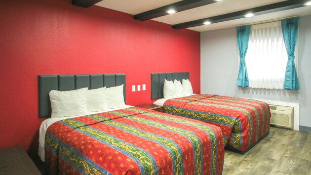 Quarto com duas camas, paredes vermelhas e uma janela com cortinas azuis.