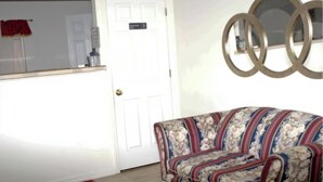 Uma sala de estar com um sofá floral, uma porta branca e um espelho circular fixado na parede.