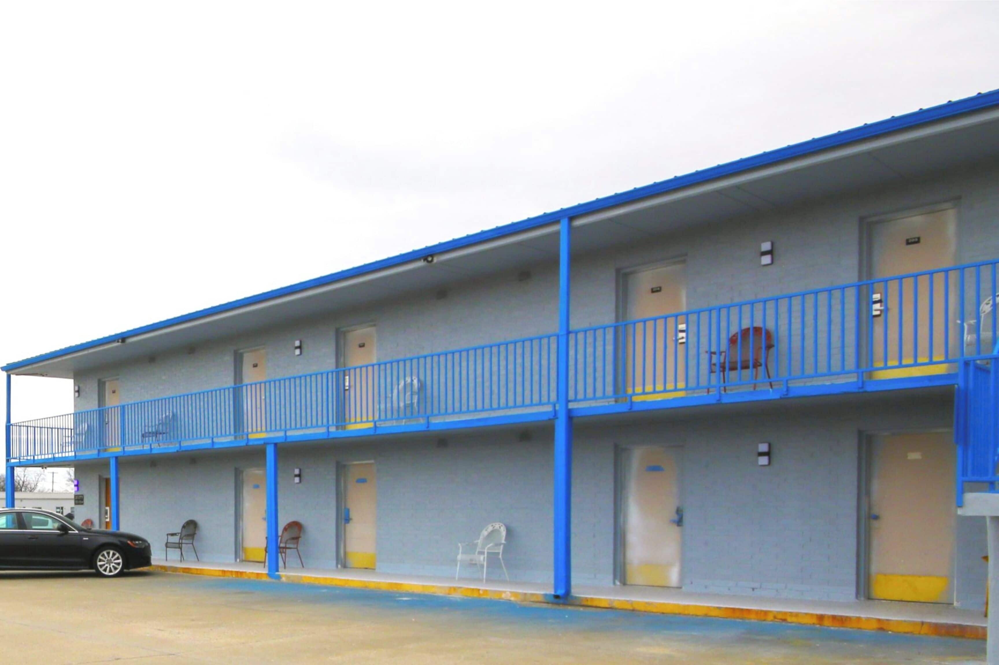 Um motel com fachada azul, várias divisões e um carro estacionado em frente.