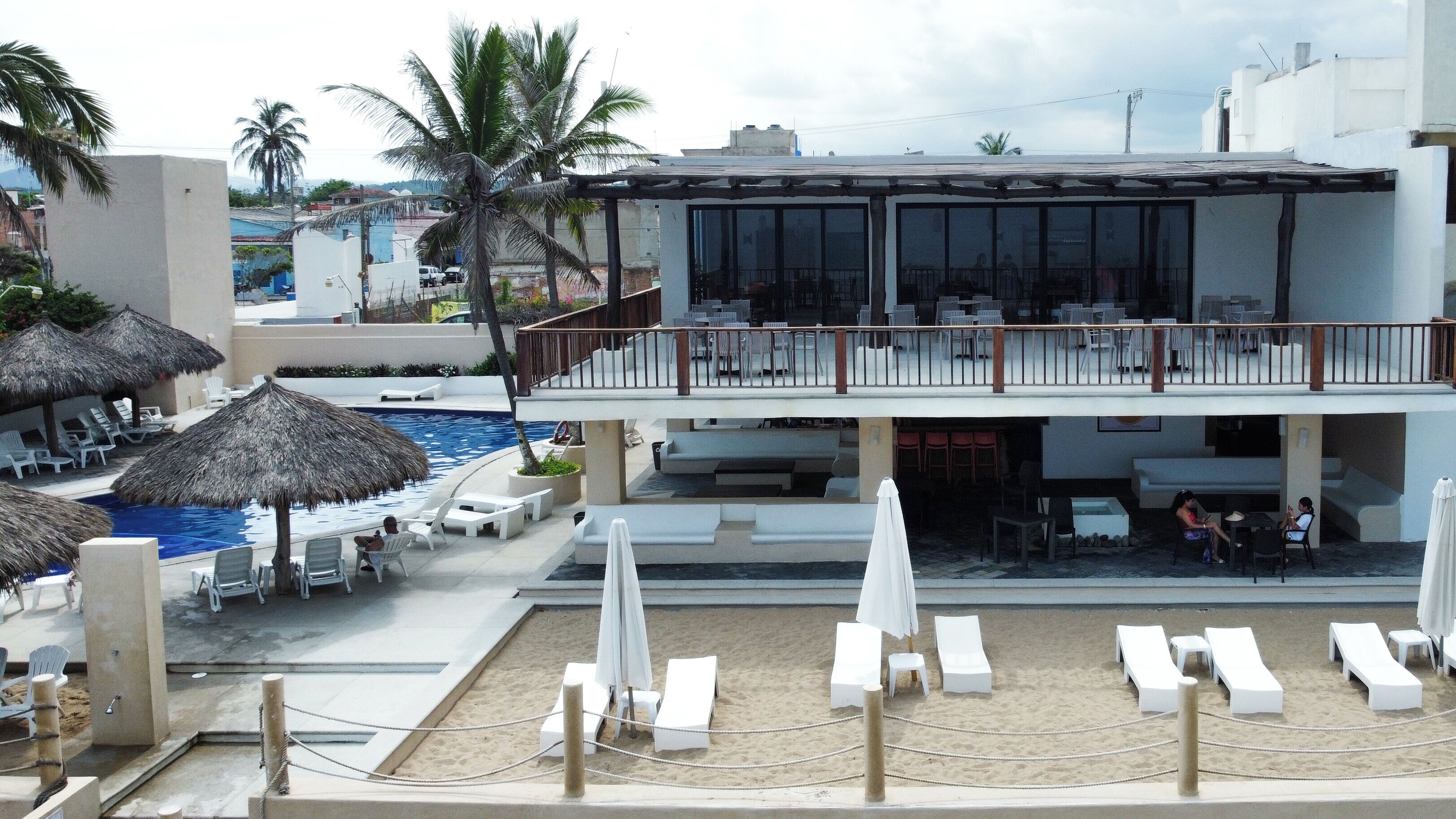 Resort com piscina, espreguiçadeiras, guarda-sóis e área de refeições.