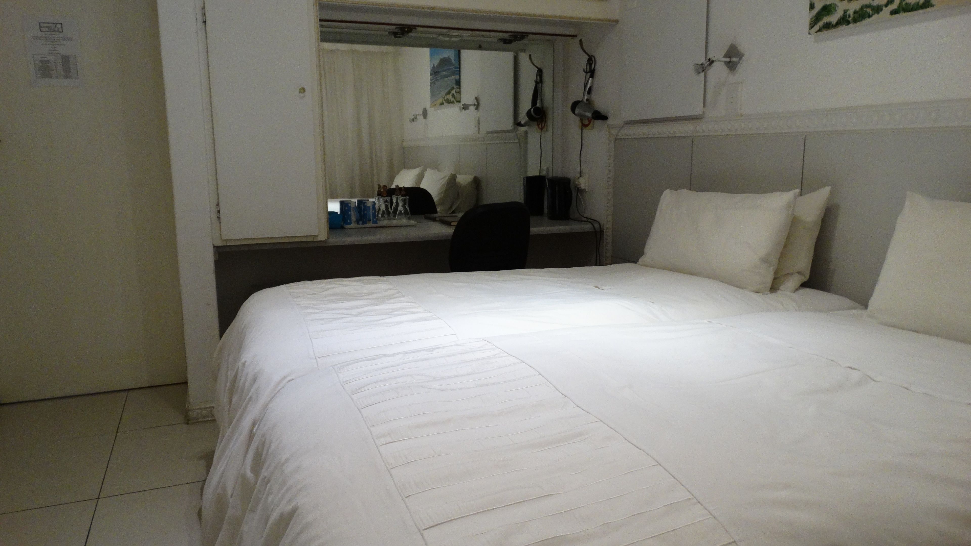 Quarto de hotel com uma cama grande, uma escrivaninha com computador e uma cadeira.