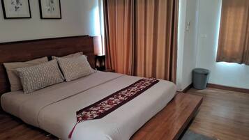 Cama bem arrumada com colcha estampada e almofadas, cabeceira de madeira e mesa de cabeceira com abajur.