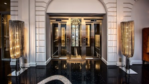 Entrada de elevador com design moderno, duas colunas decorativas grandes e piso preto polido.