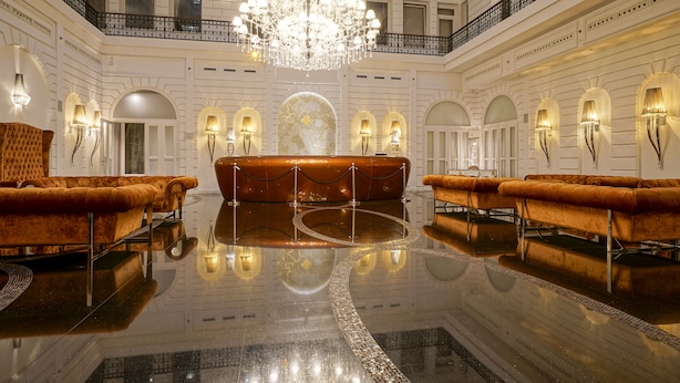Um hall luxuoso com um lustre imponente, assentos confortáveis e elegantes arandelas.