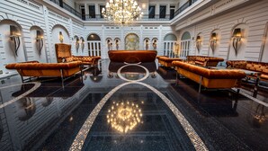 Um lobby de hotel luxuoso com um lustre imponente, assentos confortáveis e um piso preto espelhado.