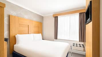 Quarto de hotel com uma cama grande, televisão fixada na parede e janela com cortinas.