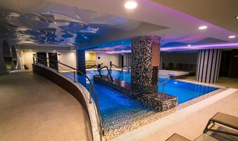 Piscina interior moderna com um design de mosaico único, área de estar e escadaria que dá acesso a um nível superior.