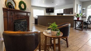 Uma sala de estar moderna com lareira, poltronas de couro, uma mesa de centro e uma cozinha ao fundo.