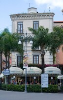 Edifício com fachada clássica, área externa com mesas e guarda-sóis, e uma placa indicando atrações próximas.