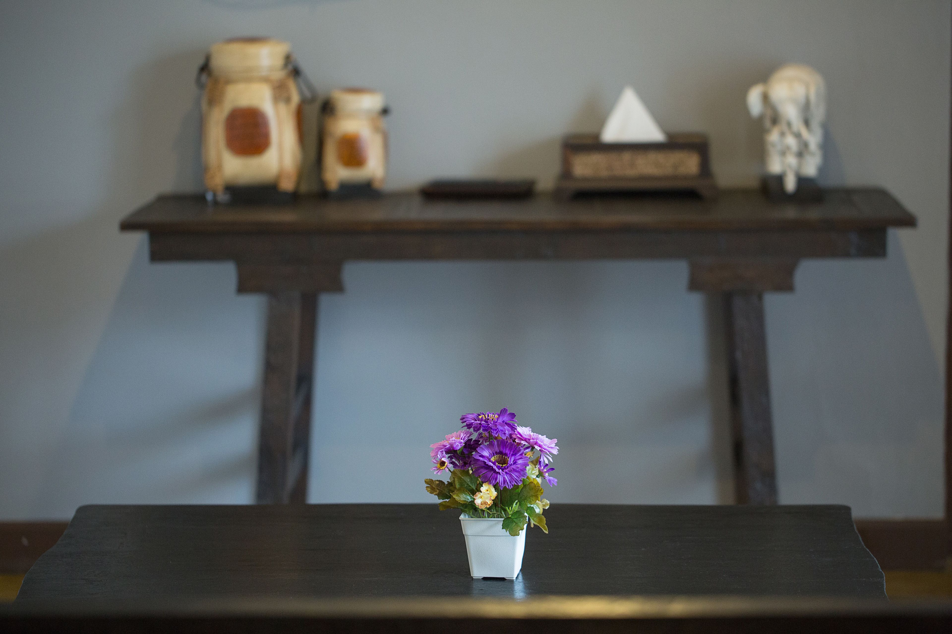 Um pequeno vaso branco com flores roxas sobre uma mesa de madeira escura.