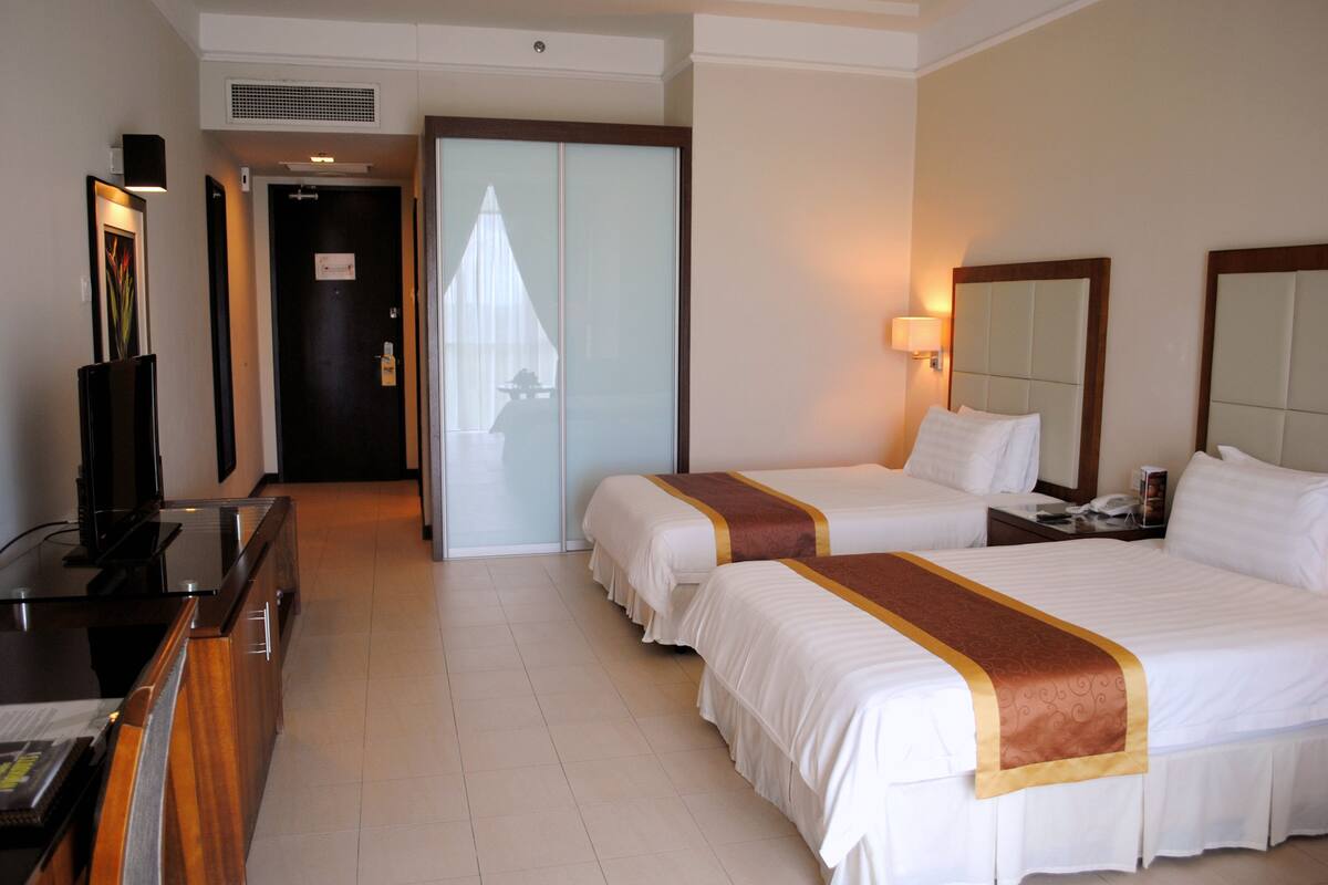 Quarto de hotel com duas camas, uma escrivaninha, uma televisão e uma porta de correr.
