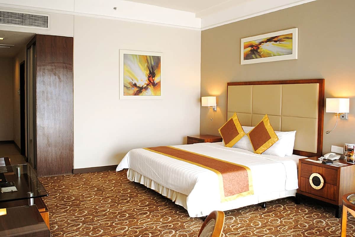 Quarto de hotel com uma cama grande, uma escrivaninha, televisão e obras de arte nas paredes.