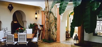 Uma área de refeições com mesa e cadeiras, uma parede decorativa com uma planta e um candeeiro.