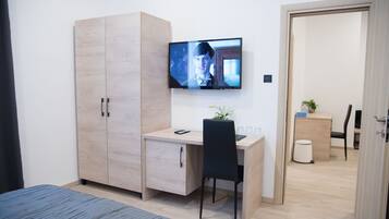 Um quarto com uma cama, uma escrivaninha com cadeira, uma TV na parede e um guarda-roupa.