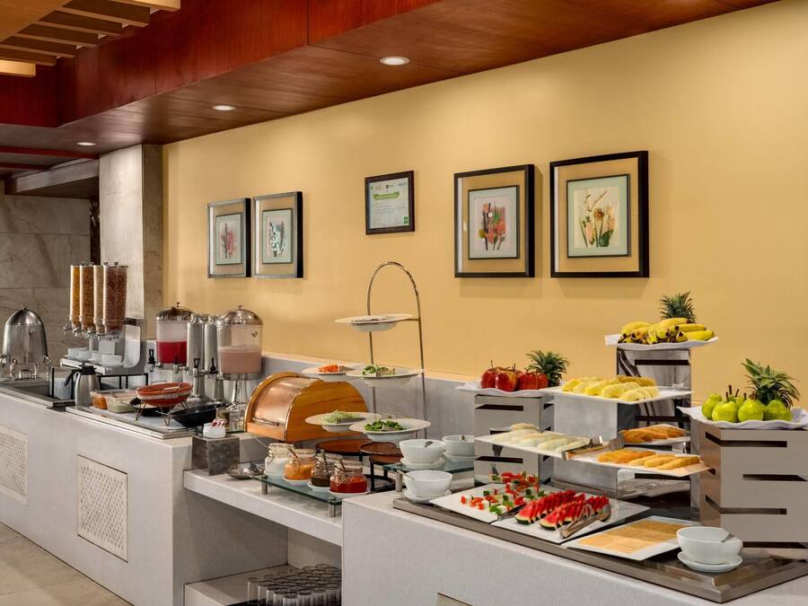 Disposição de buffet com diversos alimentos e bebidas, incluindo frutas, doces e um espaço para café.
