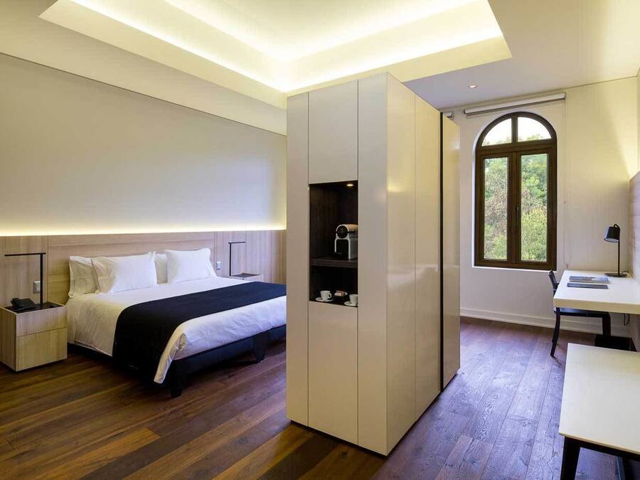 Quarto de hotel moderno com cama, mesa de cabeceira, escrivaninha e guarda-roupa.