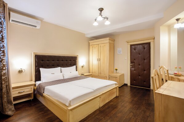 Quarto de hotel com cama grande, guarda-roupa de madeira, mesas de cabeceira e uma escrivaninha com cadeiras.