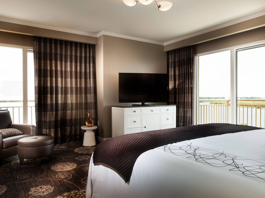Quarto de hotel com uma cama grande, televisão de tela plana, sofá e vista para o exterior.