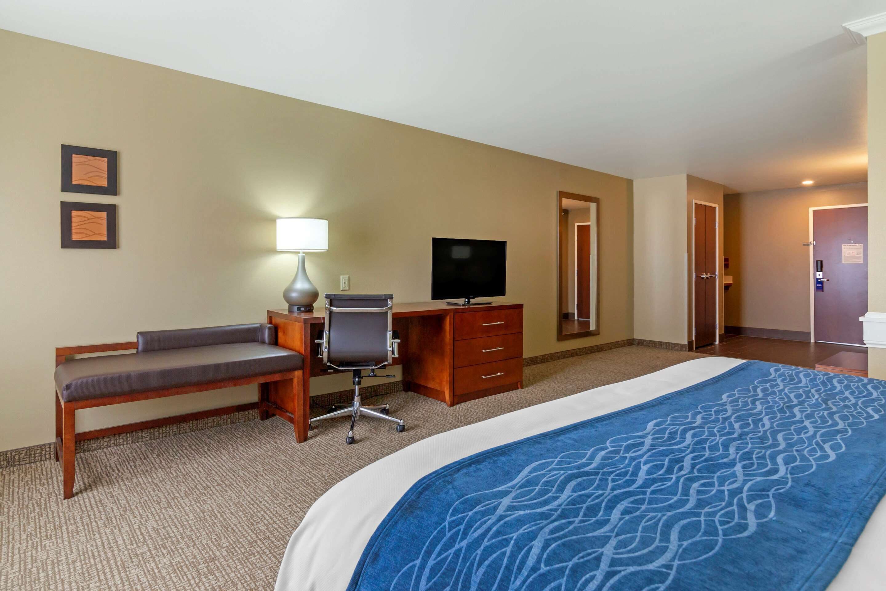 Quarto de hotel com cama, escrivaninha, cadeira, televisão e um banco.