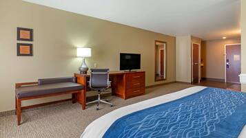 Quarto de hotel com cama, escrivaninha, cadeira, televisão e um banco.