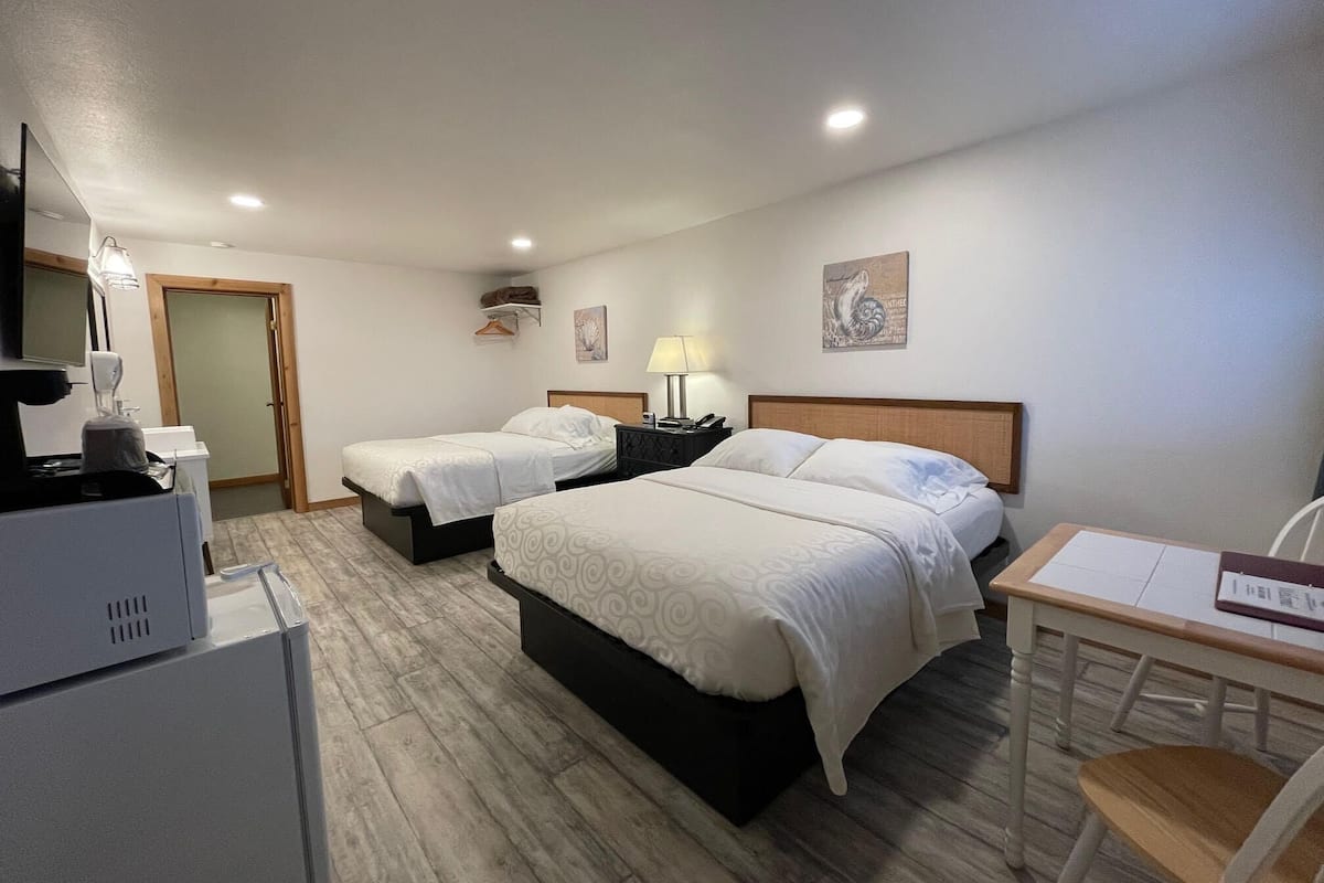 Quarto de hotel com duas camas, uma mesa, uma cadeira, uma televisão e um micro-ondas.