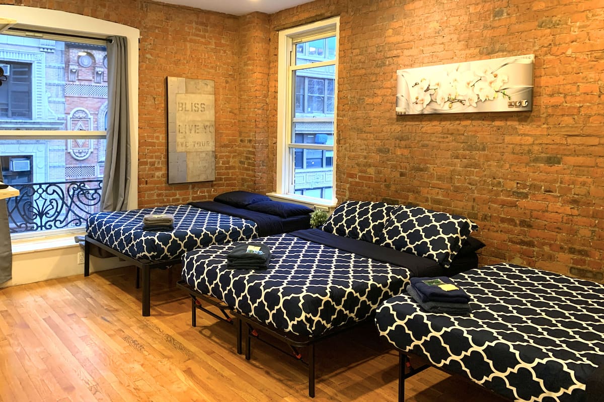 Quarto com duas camas, parede de tijolos e janela com vista para edifícios.