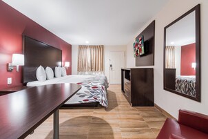 Quarto de hotel com cama, escrivaninha, televisão e um espelho grande.