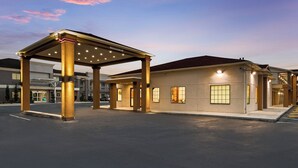 Entrada de hotel com área de espera coberta e um edifício com várias janelas.