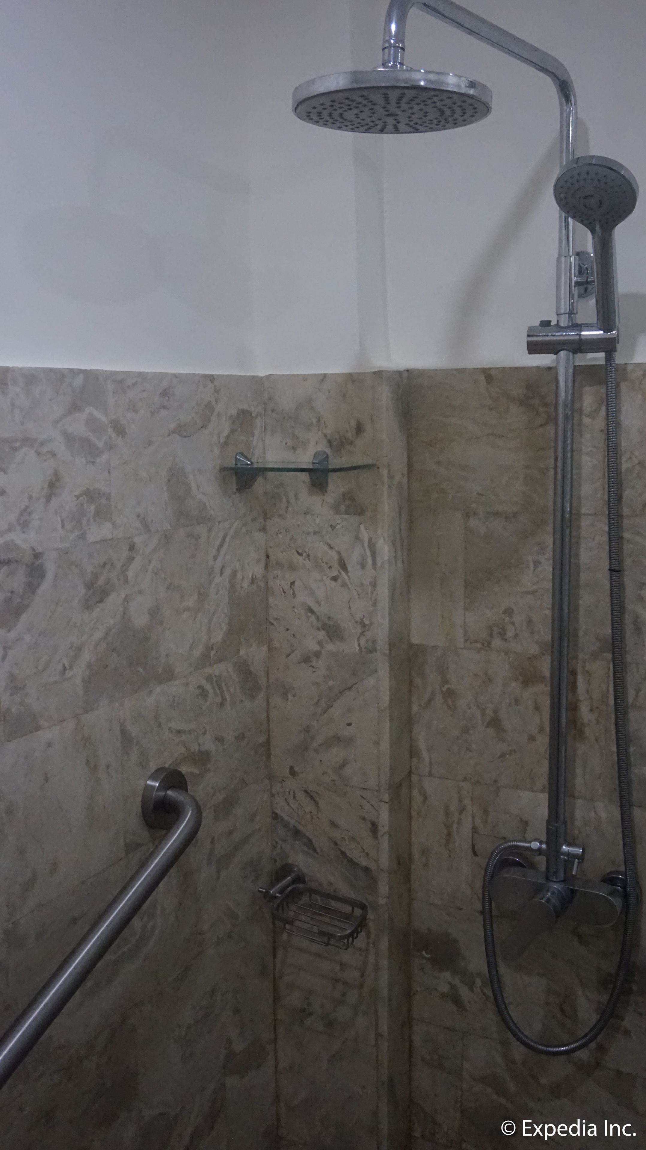 Uma área de chuveiro com chuveiro manual e barra de apoio.