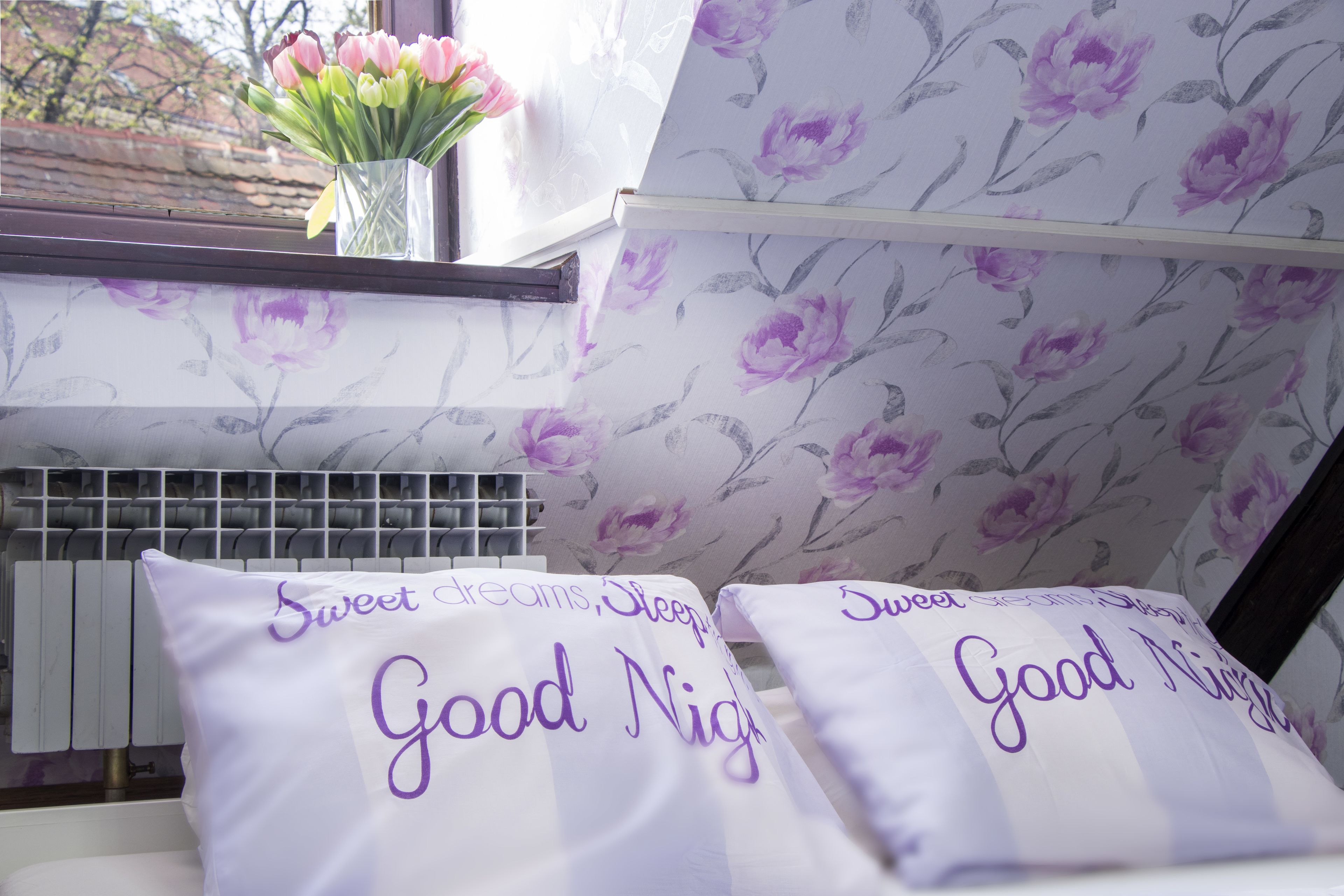 Quarto com papel de parede floral, janela com vista para árvores e almofadas com a inscrição 'Sweet Dreams, Sweet Sleep'.