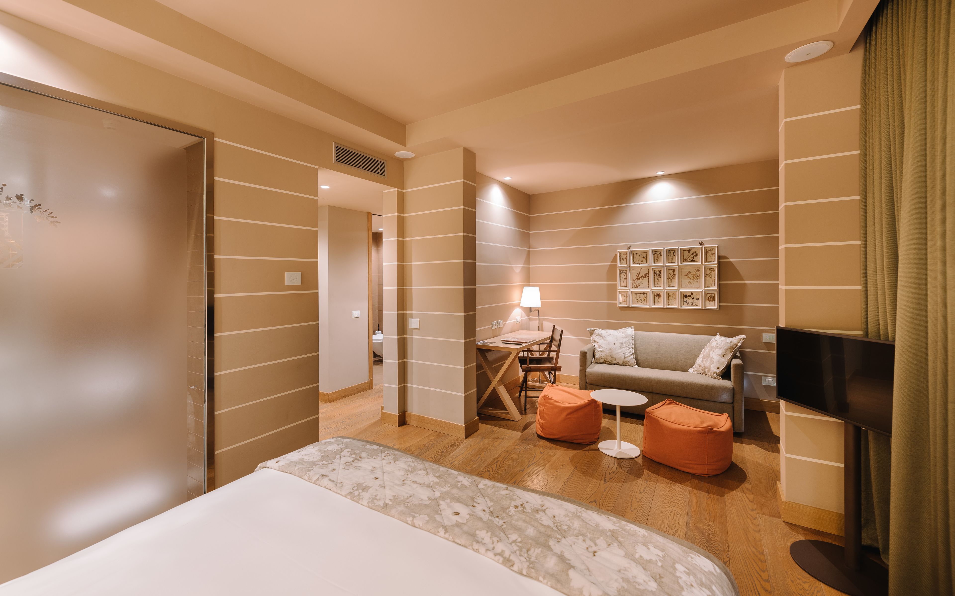 Quarto de hotel com cama, sofá, televisão e uma pequena mesa com abajur.