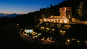 Um edifício amplo e iluminado, com vários níveis e janelas em arco, cercado por vegetação exuberante e um paisagismo em terraços.