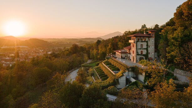 Um edifício histórico com fachada de pedra, jardins em terraços e vista do horizonte durante o pôr do sol.