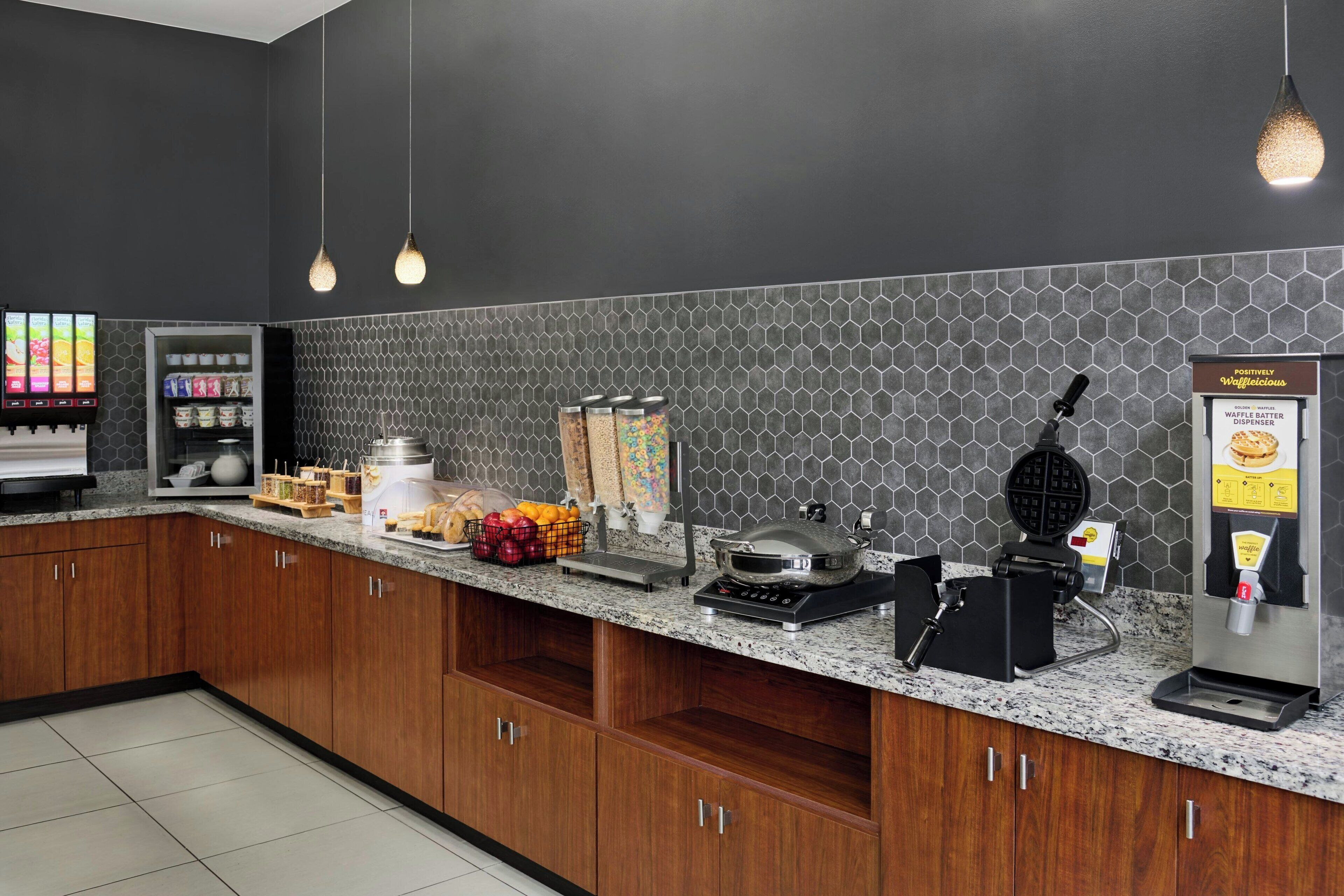 Uma cozinha moderna com bancada de granito, máquina de waffle, cafeteira e geladeira.