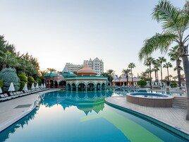 Uma grande piscina com o reflexo de um edifício e palmeiras.