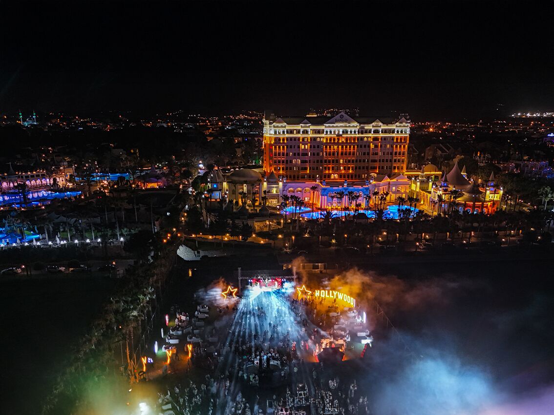 Um hotel com um edifício grande e uma área de piscina iluminada.