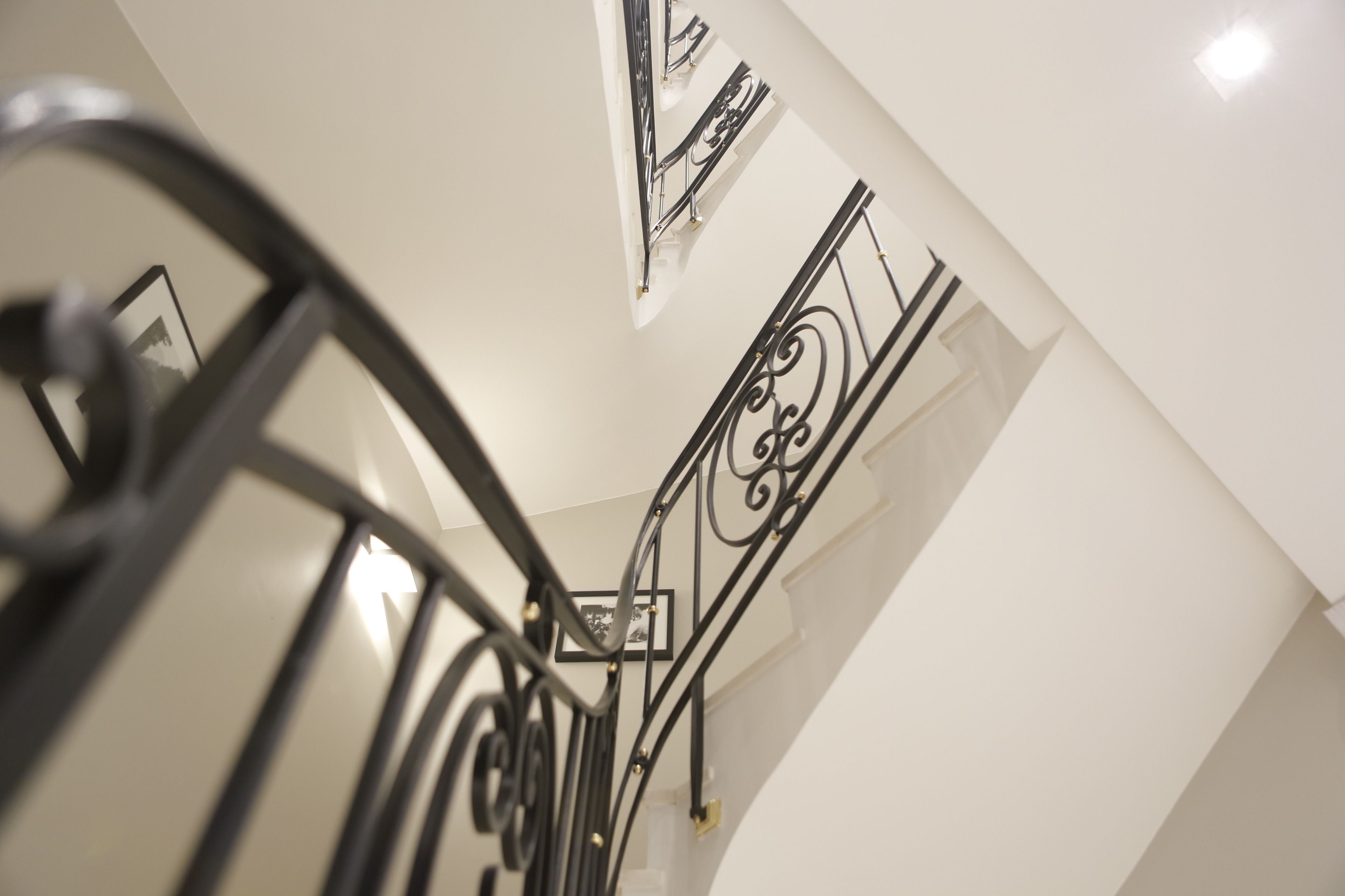 Uma escadaria com grades de metal preto decoradas e um quadro na parede.