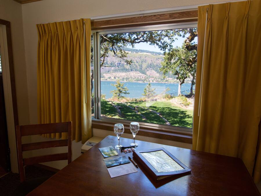 Mesa de jantar com vista para um lago e colinas, cortinas amarelas e uma moldura com imagem.