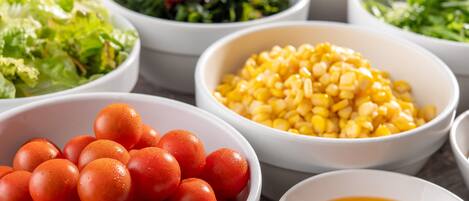 Diversos alimentos em tigelas, incluindo tomates, milho e uma salada.