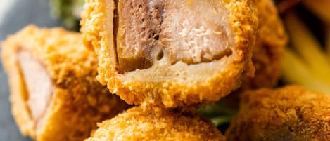 Close-up de um alimento empanado e frito, provavelmente um croquete ou prato semelhante.