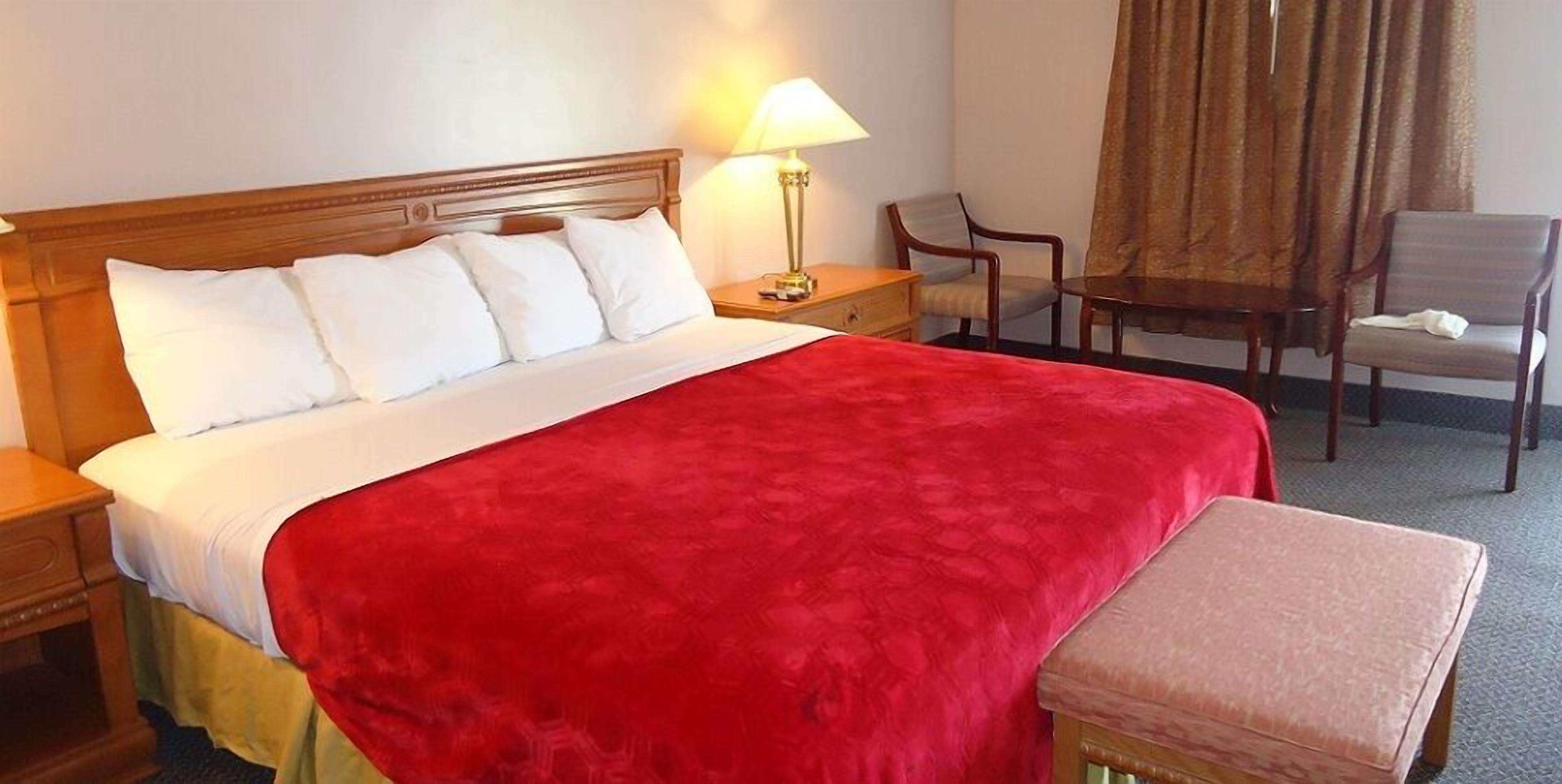 Quarto de hotel com uma cama grande, uma mesa de cabeceira, uma luminária, uma cadeira e uma pequena mesa.