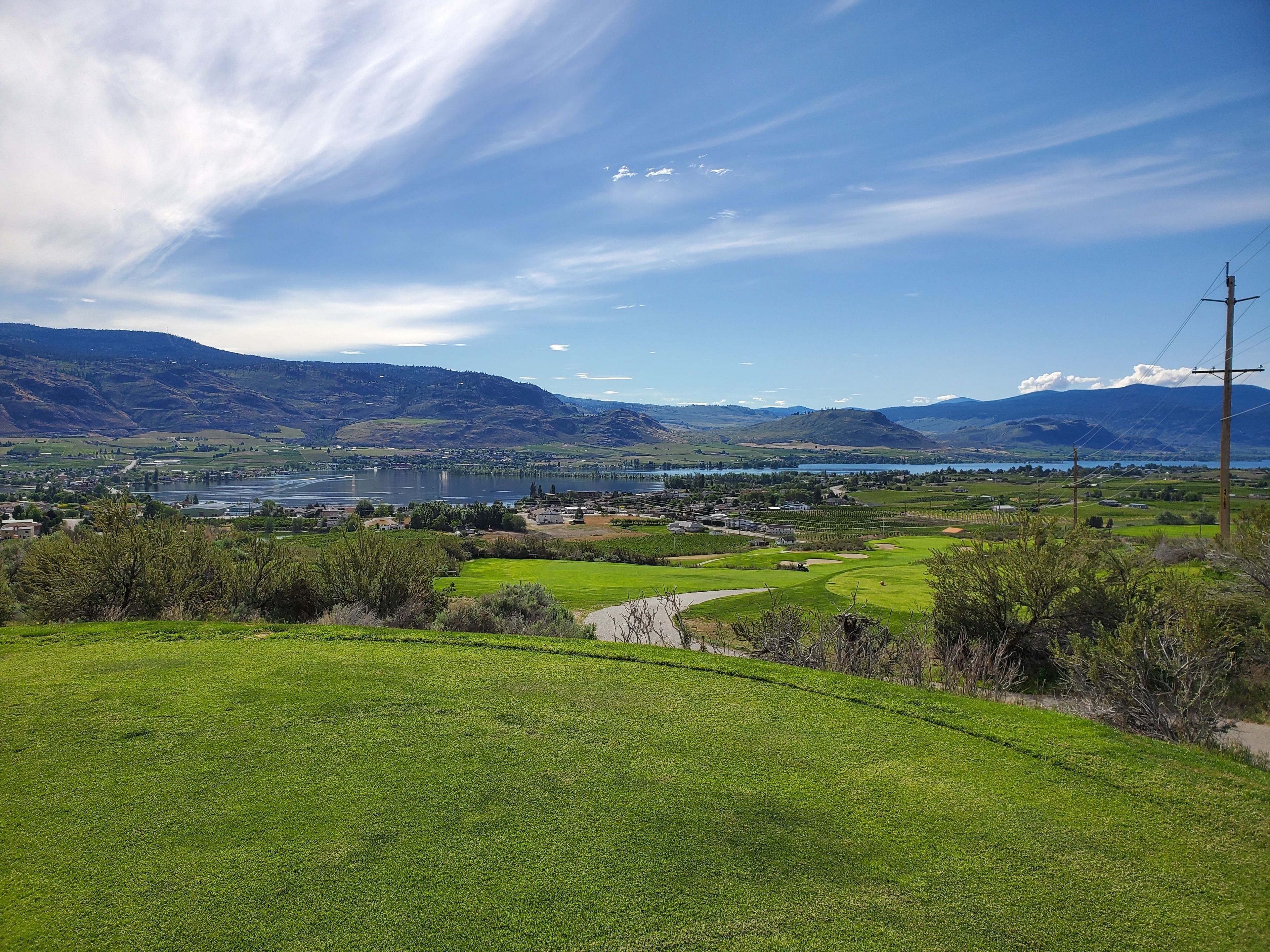 Paisagem pitoresca com um lago, montanhas e um campo de golfe.